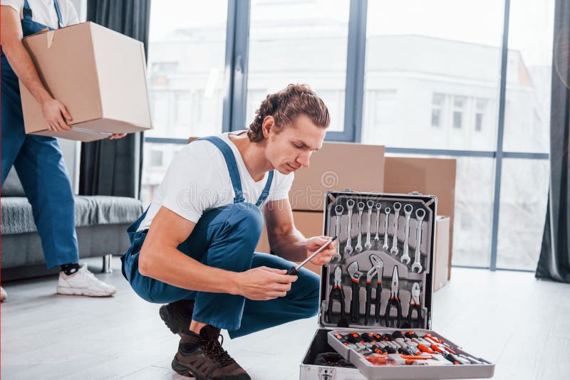 Uses Tools from Case. Two Young Movers in Blue Uniform Working Indoors ...