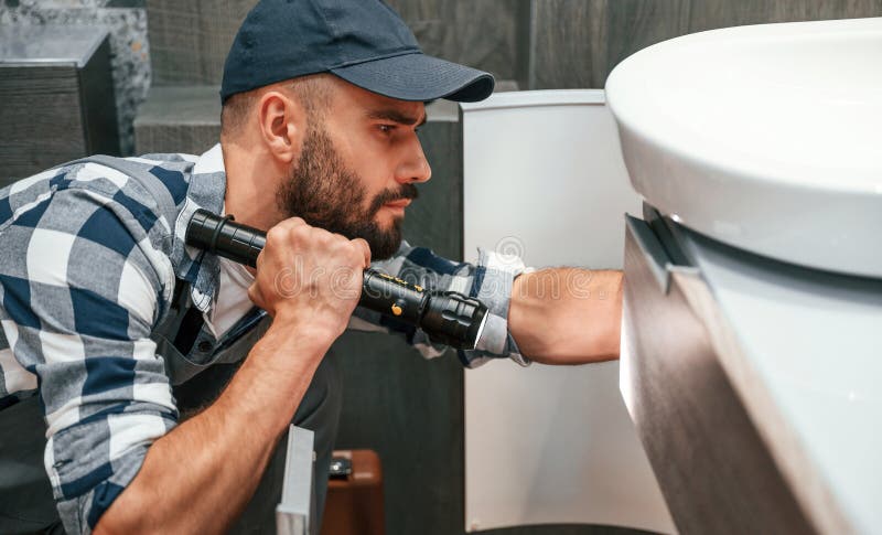 Using Flashlight. Plumber in Uniform is Indoors at Home Stock Photo ...