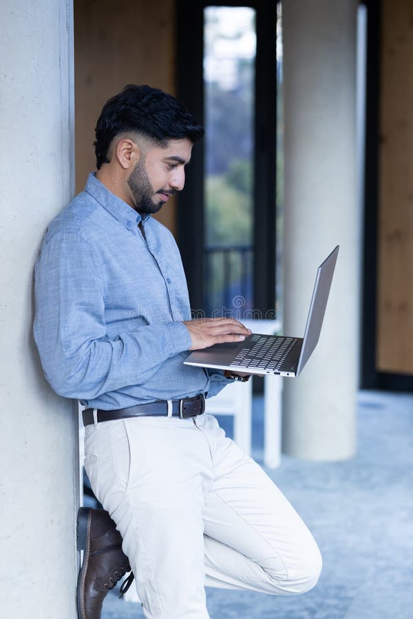 Using Laptop, Man Leaning Against Wall in Modern Office Environment ...