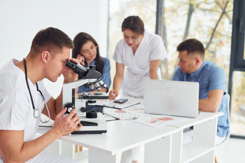 Using Microscope. Group of Young Doctors is Working Together in the ...