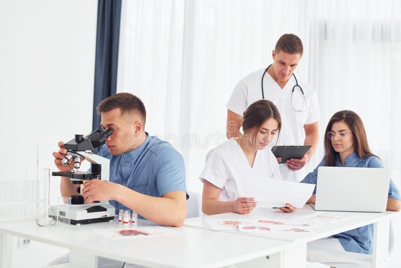 Using Microscope. Group of Young Doctors is Working Together in the ...