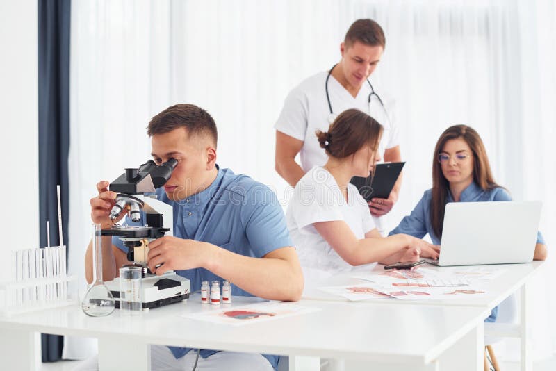 Using Microscope. Group of Young Doctors is Working Together in the ...