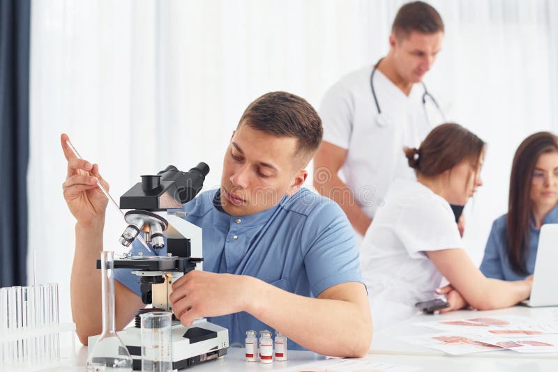 Using Microscope. Group of Young Doctors is Working Together in the ...
