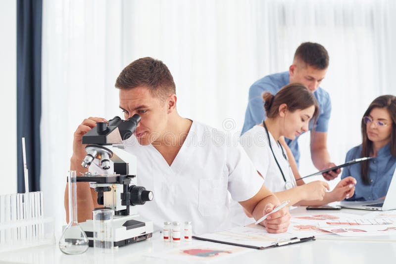 Using Microscope. Group of Young Doctors is Working Together in the ...