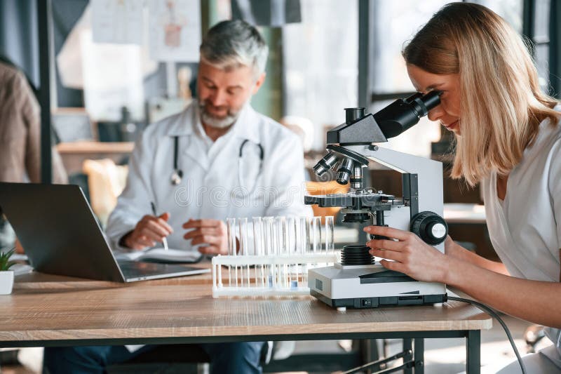 Using Microscope. Two Clinic Workers are Indoors Together. Senior Man ...