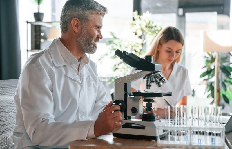 Using Microscope. Two Clinic Workers are Indoors Together. Senior Man ...
