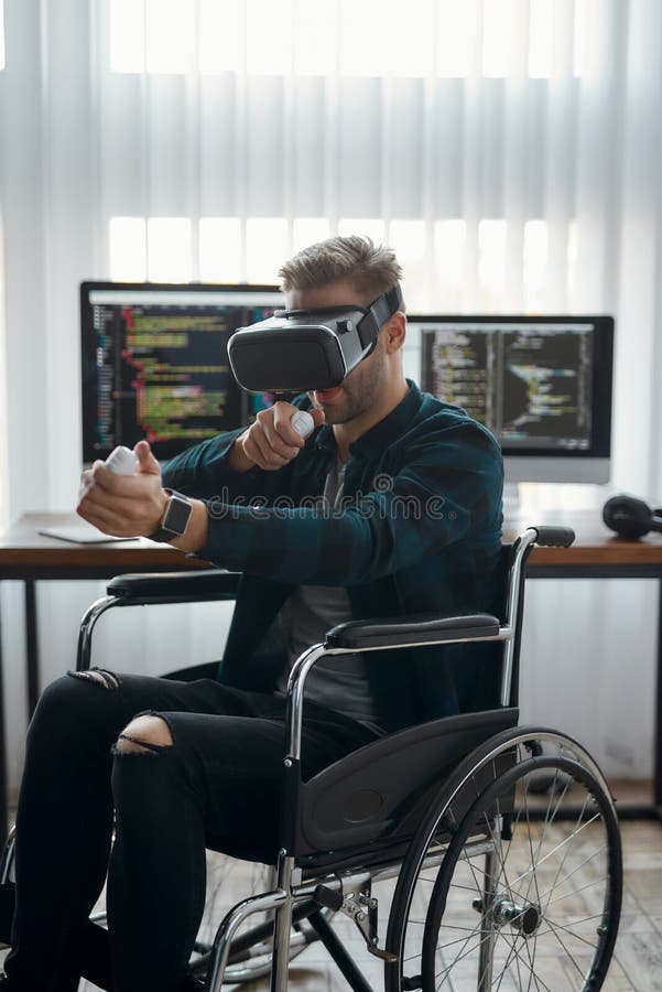 Using Modern Technologies. Young Male Web Developer in a Wheelchair Wearing Virtual Reality ...