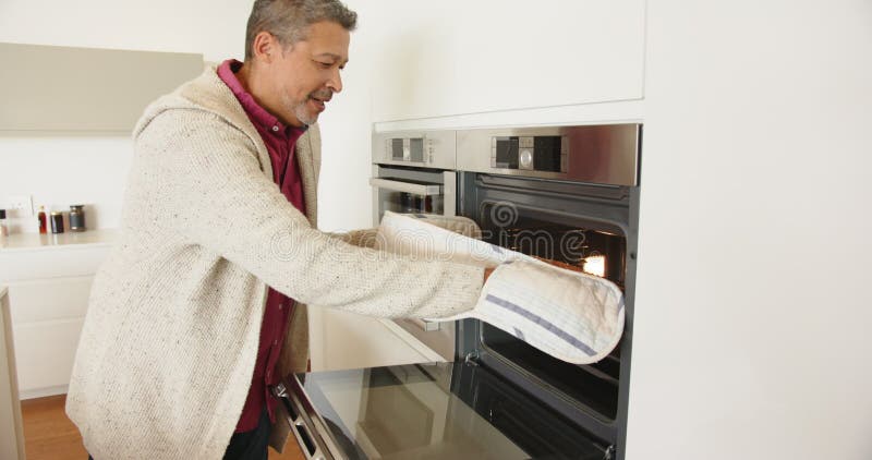 Using Oven Mitts, Man Placing Dish in Modern Kitchen Oven, Smiling, at ...