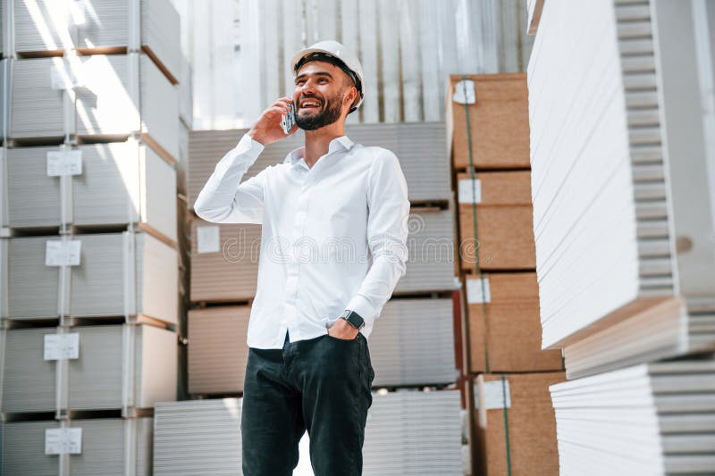 Using Phone. Storage Worker is in the Warehouse with Bunch of Products ...