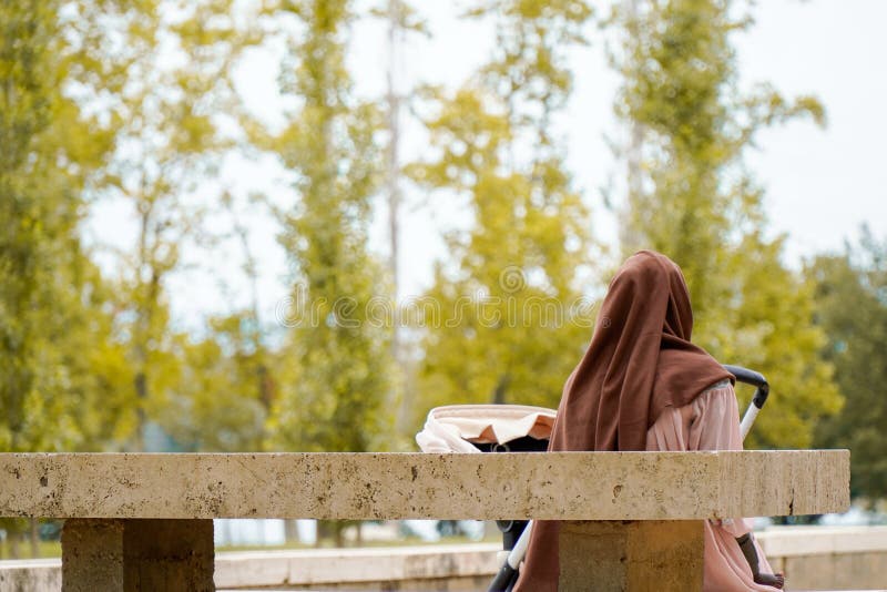 Veiled Muslim Mommy on Her Back with Her Baby in the Park. Migration in ... Veiled Muslim Mommy on Her Back with Her Baby in the Park. Migration in ...
