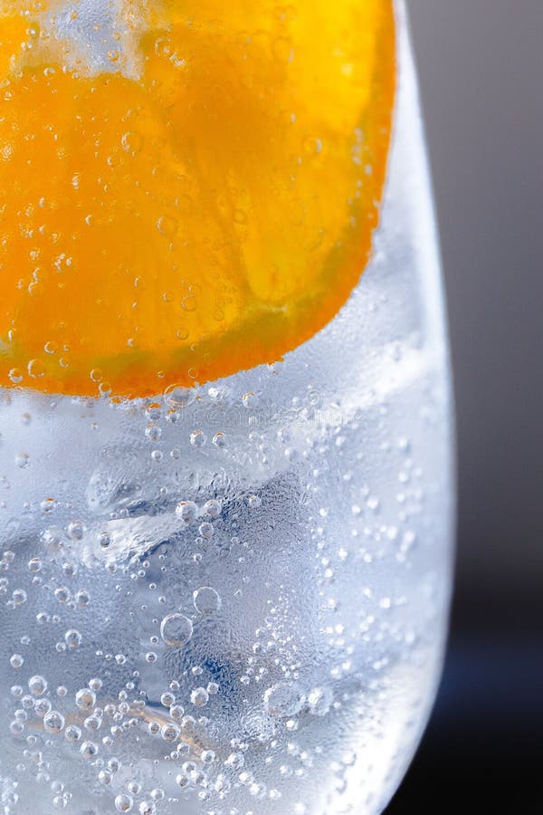 Vertical Close-up View of an Orange Slice in a Class with Bubbly Cold ...