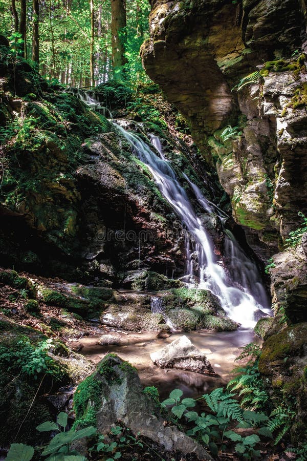 Vertical of a Waterfall Cascading Down the Rocks in a Sunny Forest ...