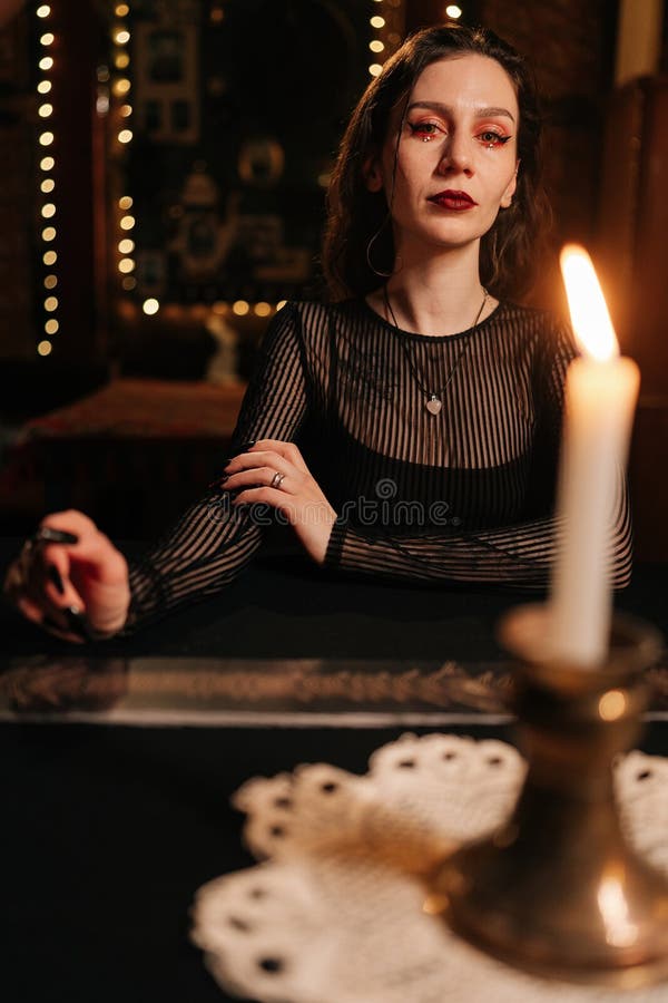Vertical Portrait of Mysterious Fortune Teller in Black Robe Sitting at Table in Dark Esoteric ...