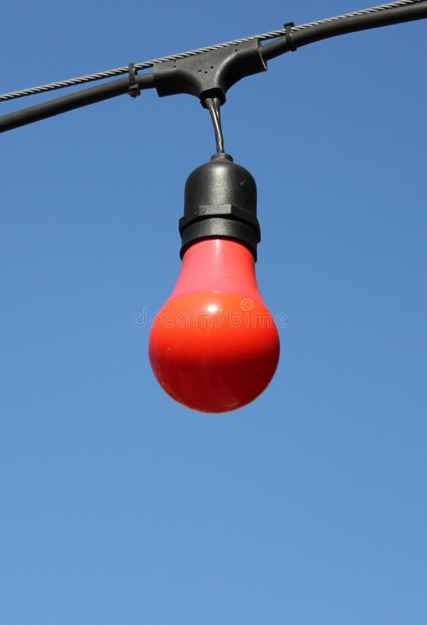 Vertical of a Red Light Bulb Hanging on a Cable Against a Vibrant Blue ...