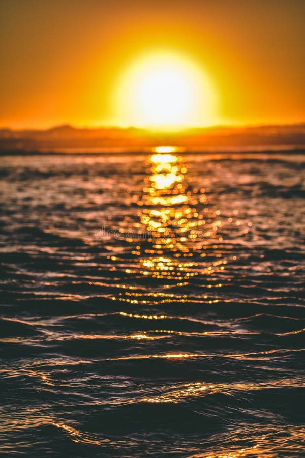 Vertical Shot of a Bright Sunset Sun Reflected on Calm Ocean during a ...