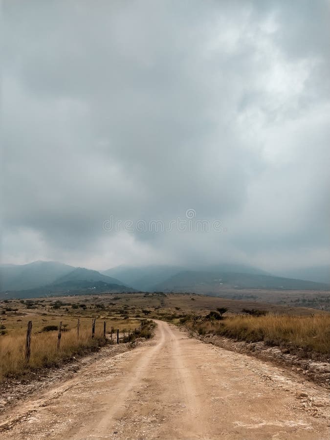 Vertical Shot of a Brown Road Leading To Distant Misty Hills Stock ...