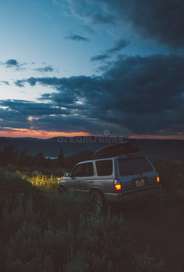 Vertical Shot of a Car in the Middle of Grassy Fields Under a Cloudy ...