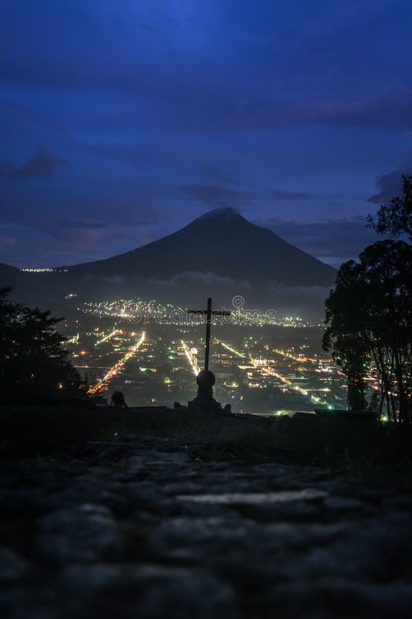 Vertical Shot of a Cross in the Background of City Lights and Mountain ...