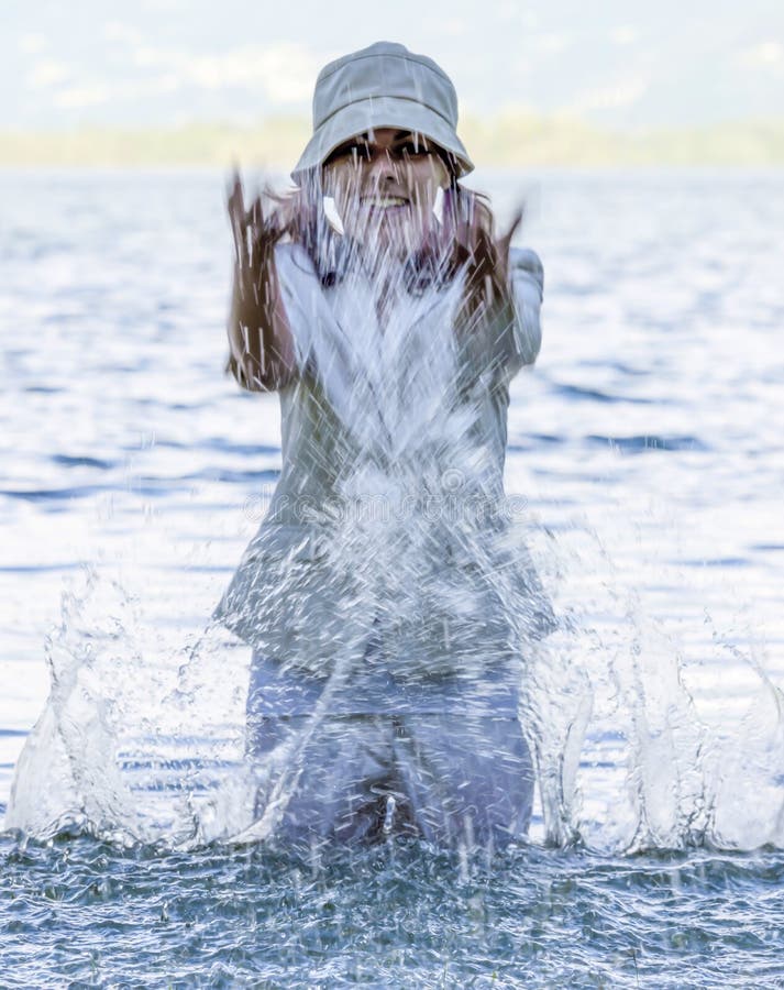 Vertical Shot of a Female Child with a Hat Making Waves in the Sea ...