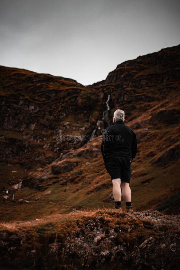 Vertical Shot of a Man Standing in Front of a Hill and Looking at it ...