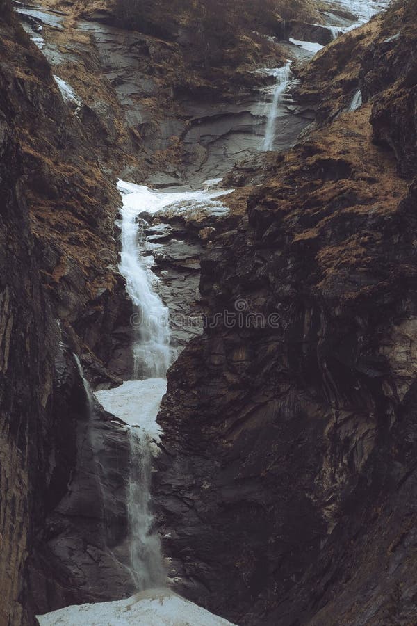 Vertical Shot of a Narrow Waterfall Route Cascading Over Rugged Cliffs ...