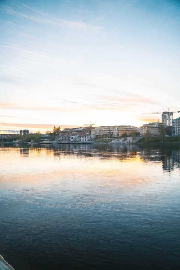 Vertical Shot of a Peaceful River at Sunset with Town Architecture ...