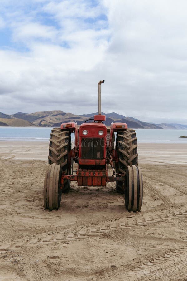 Vertical Shot of a Red Tractor on the Sand with Mountains and Lake on ...