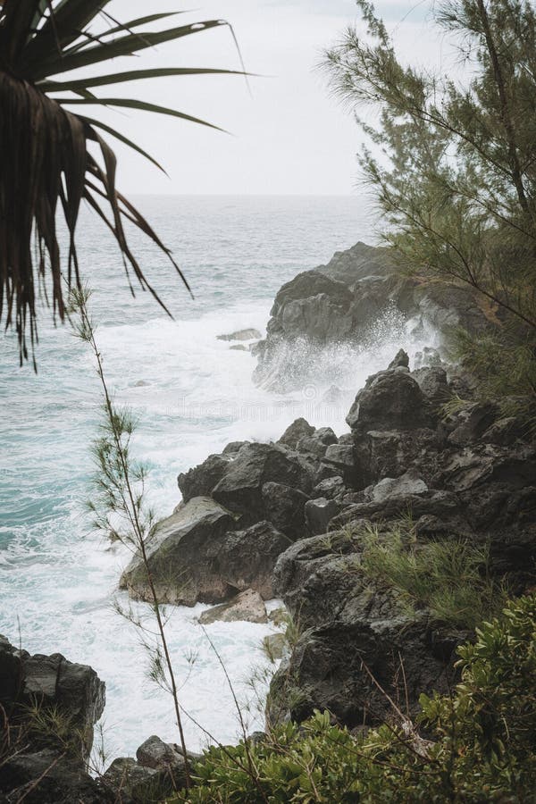 Vertical Shot of a Seashore with Foamy Waves Splashing Over the Rocks ...