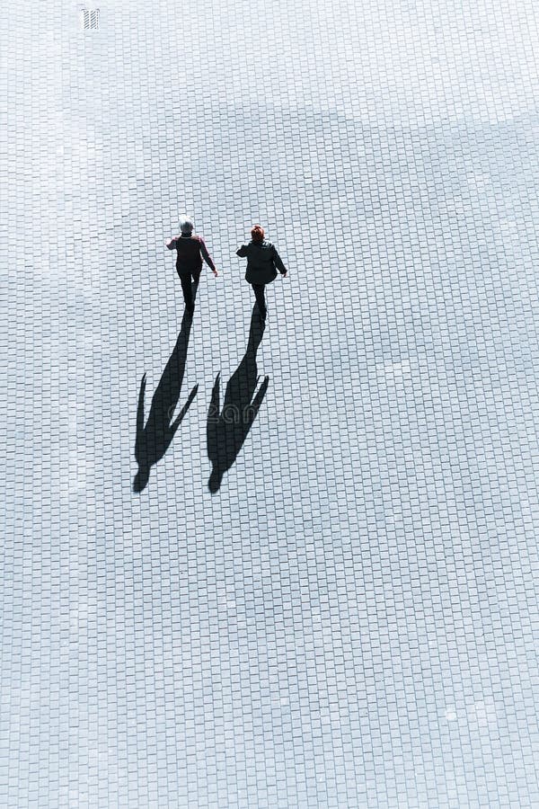 Vertical Shot of Two People Walking on the Street with Shadows on the ... Vertical Shot of Two People Walking on the Street with Shadows on the ...