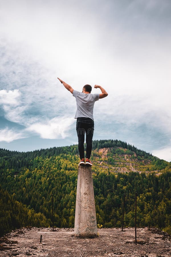 Vertical Shot of a Young Male Posing on a Platform Surrounded by Hills ...