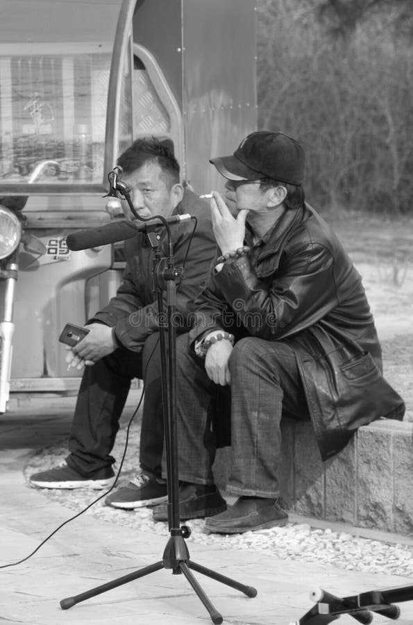 Vertical of Two Men One of Whose is Smoking Sitting in the Street with ...