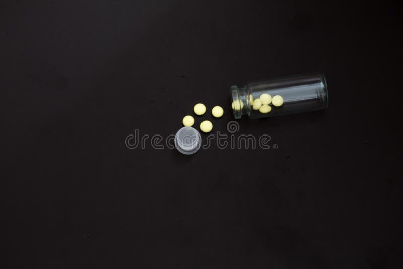 A Vial Bottle with an Open Lid with Yellow Tablets Inside on a Black ...