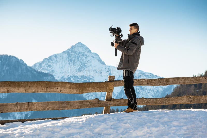 Videographer Man Shooting Footage in Snow and Mountains in Background ...