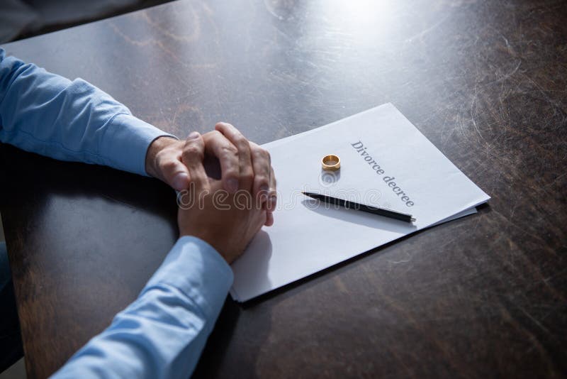 View of Man Sitting at Table with Clenched Hands with Divorce Documents ...