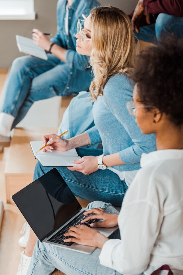 View of Multiethnic Students Writing in Notebooks and Using Laptop in ...