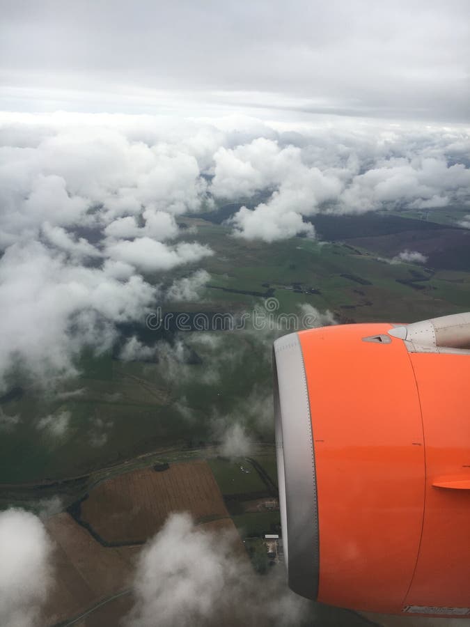 View from an Orange Airplane Over the Clouds and Land Stock Photo ...