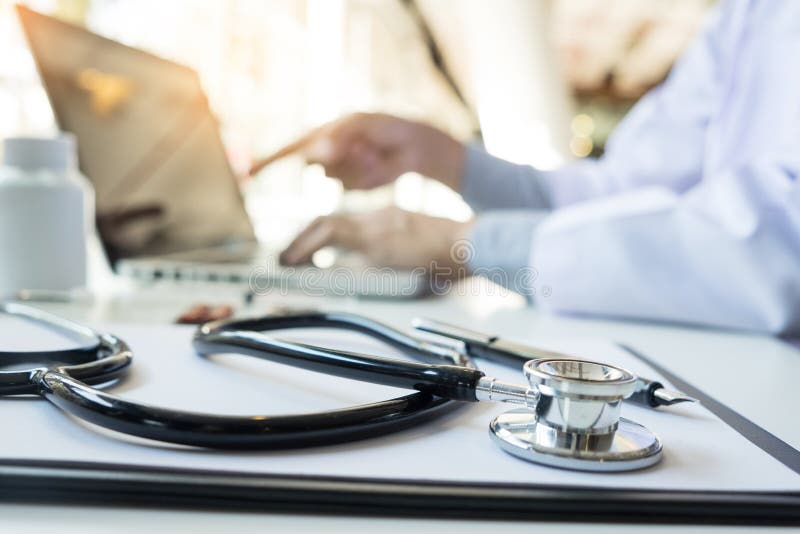 View of Stethoscope and Equipment on Foreground Table with Doctor Using ...