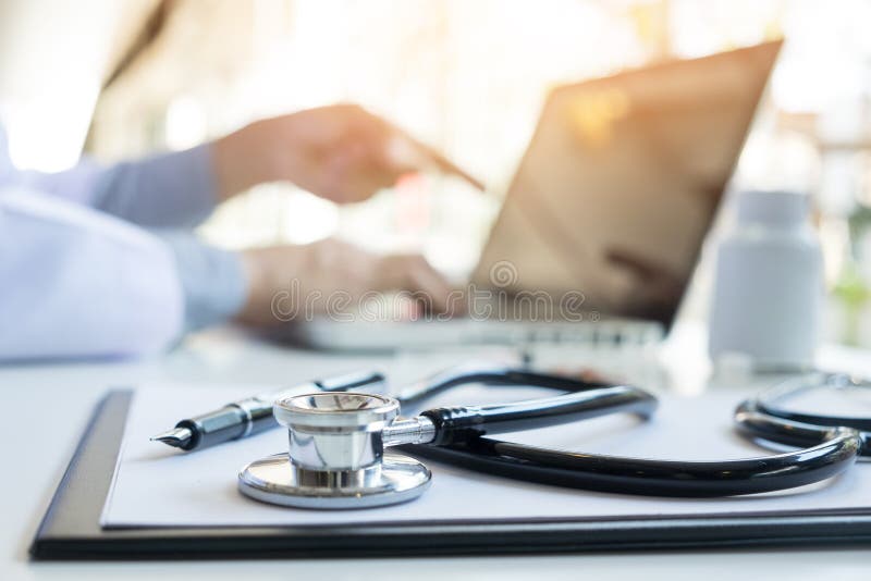 View of Stethoscope and Equipment on Foreground Table with Doctor Using ...