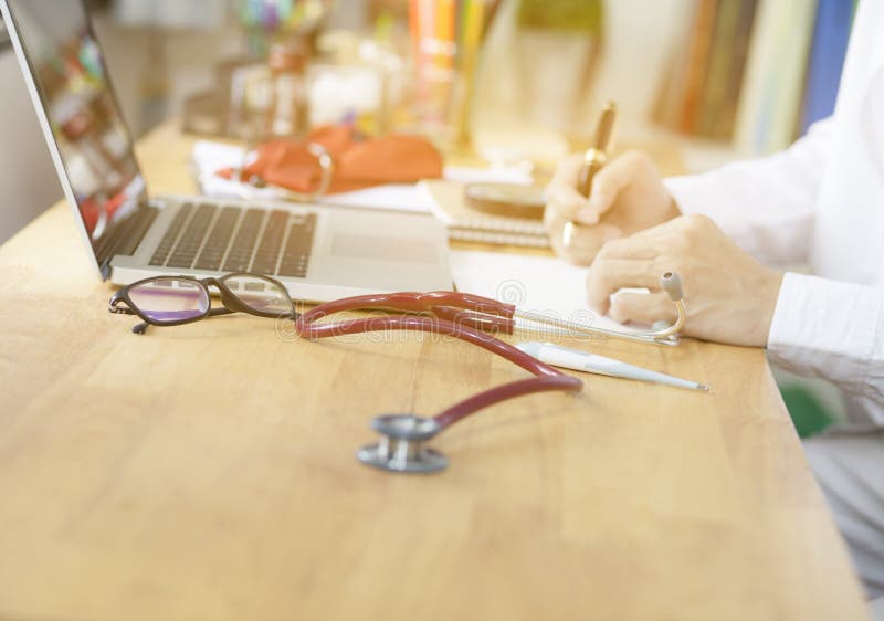 View of Stethoscope and Equipment on Foreground Table with Doctor Using ...