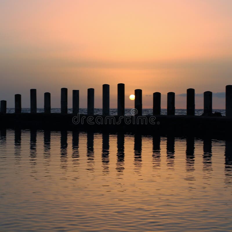 View of the Sunset with Vertical Poles on the Shore and Reflections in ...