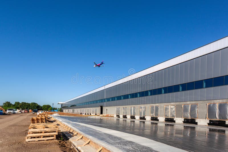 View of a Warehouse with an Airplane Flying Over it on a Blue Sky ...