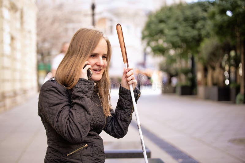 A Visually Impaired Woman Standing in City with a White Cane and Using ...