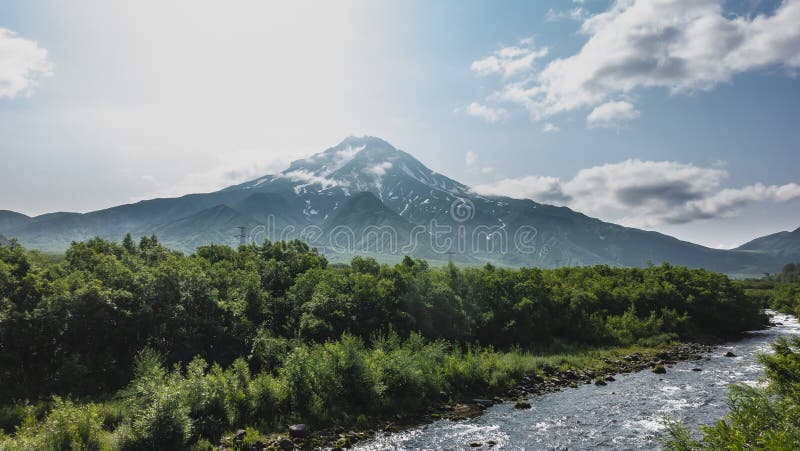 A Volcano with a Snow-capped Peak on the Background of a Blue Sky with ...