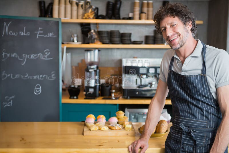 Male Barista Wearing Apron Leaning on Cafe Counter Showing Pastries ...