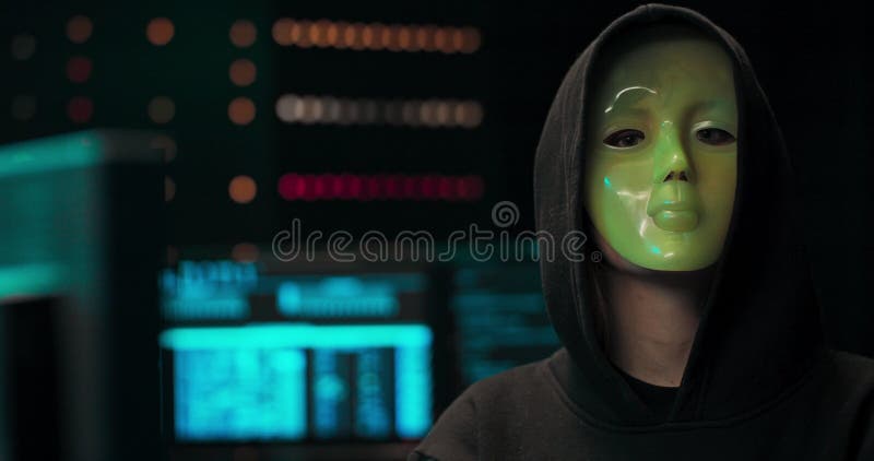 Wanted Hacker with Masked Face Looks into the Camera in the Background ...