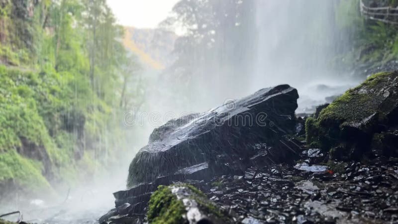 A Large, Black Boulder Rests at the Base of the Waterfall, and a Swift ...
