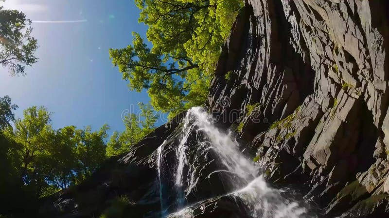 Waterfall Cascading Down Rocky Cliff with Green Forest and Blue Sky ...