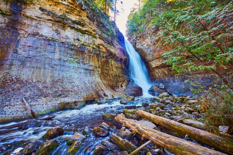 Waterfall Over Tall Cliffs in Canyon with Greenery and Driftwood in a ...
