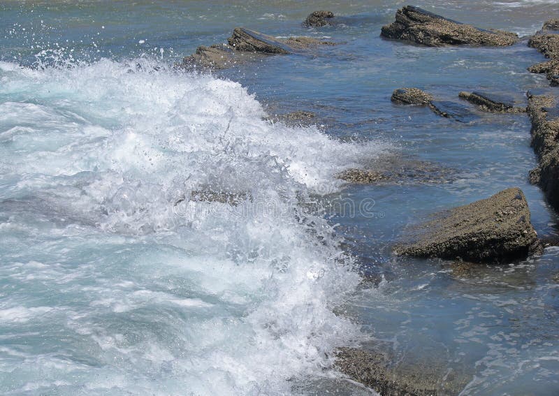 TURQUOISE SEAWATER PUSHING OUT ONTO SAND OVER ROCKS Stock Image - Image ...