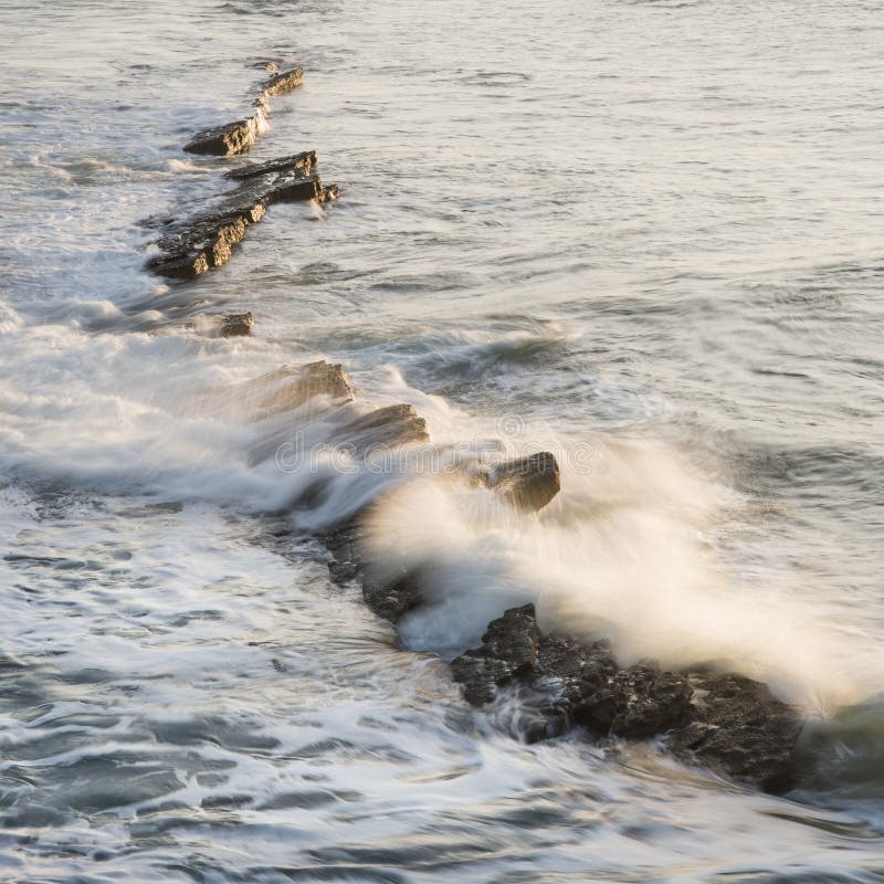 Wave Crashing Over Rocks in Ocean at Sunrise with Long Exposure Stock ...